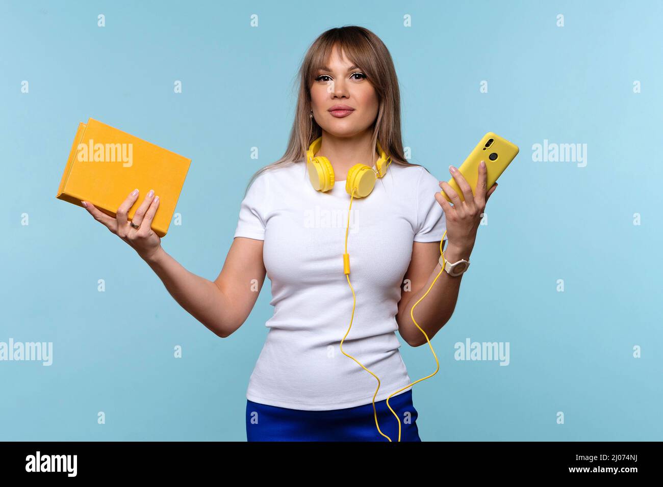Pretty young woman in yellow headphones holding yellow paper book and ...