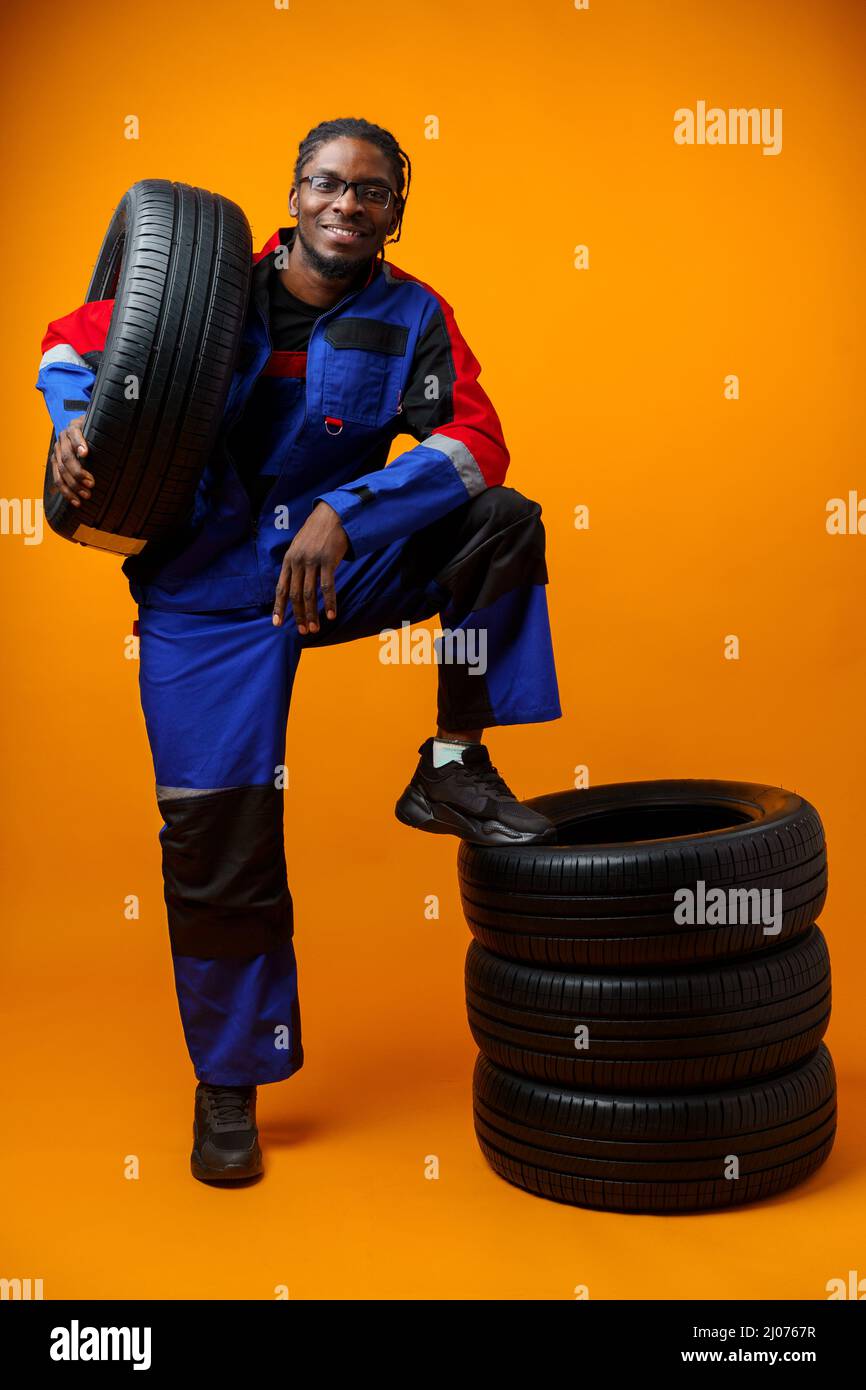 African american car service worker with car tyre against yellow ...