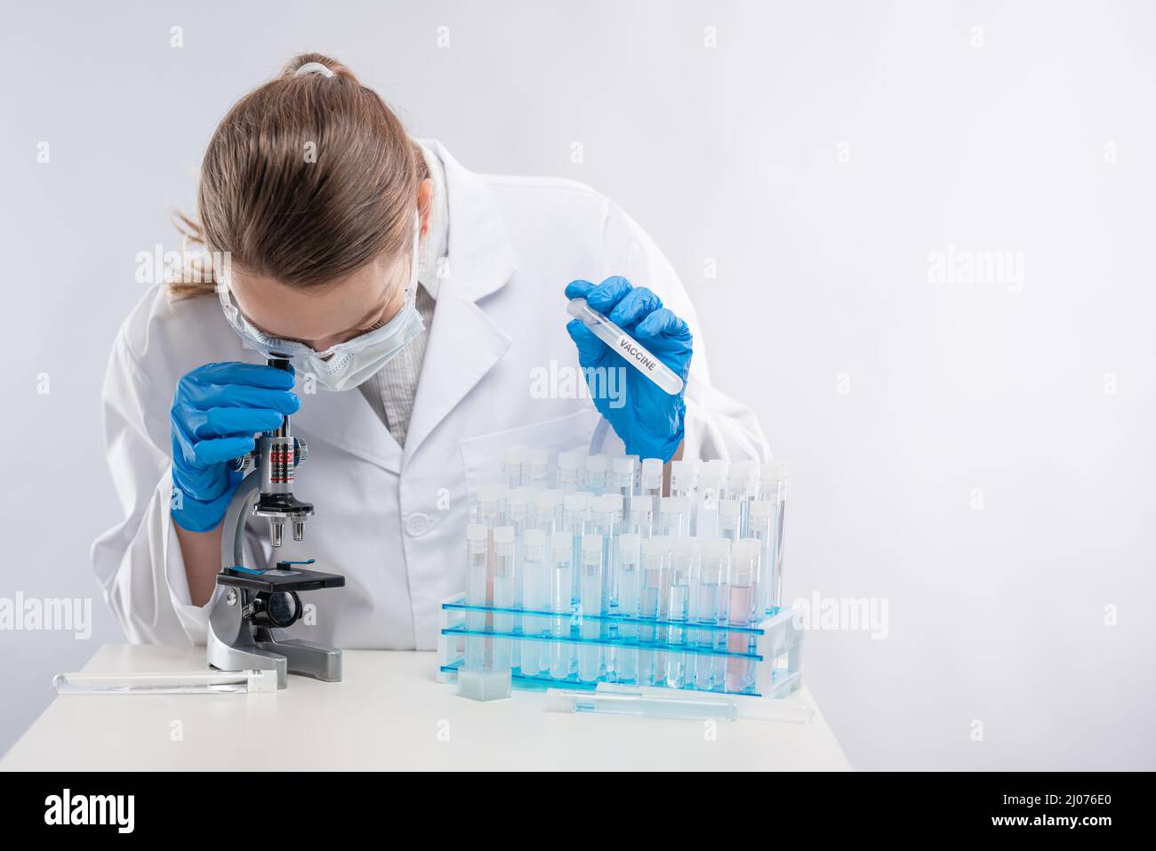 Female microbiologist in protective gloves and face mask use microscope ...