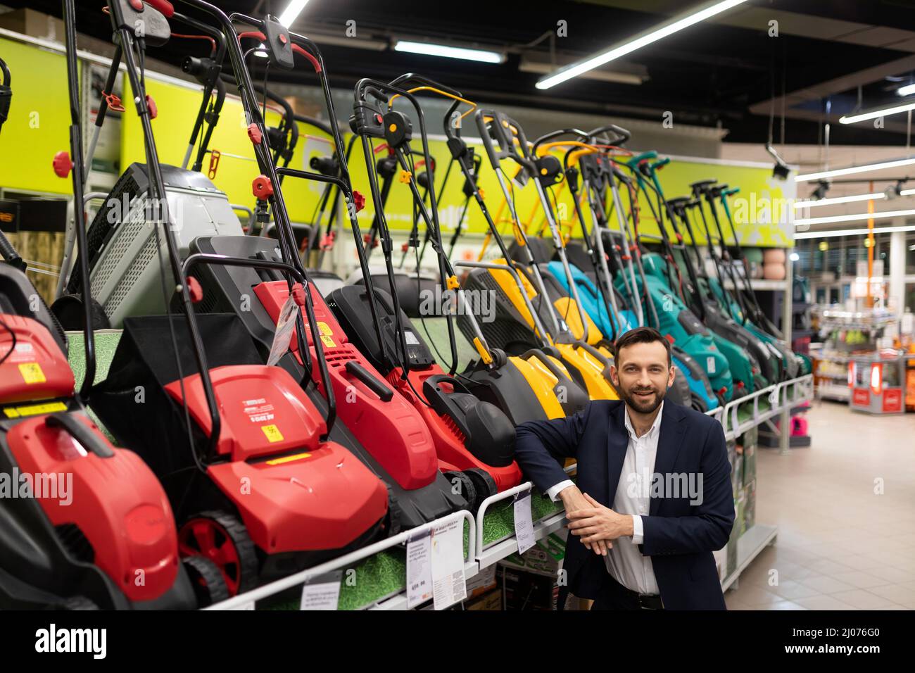 Owner of a gardening power tool store next to a display case with ...