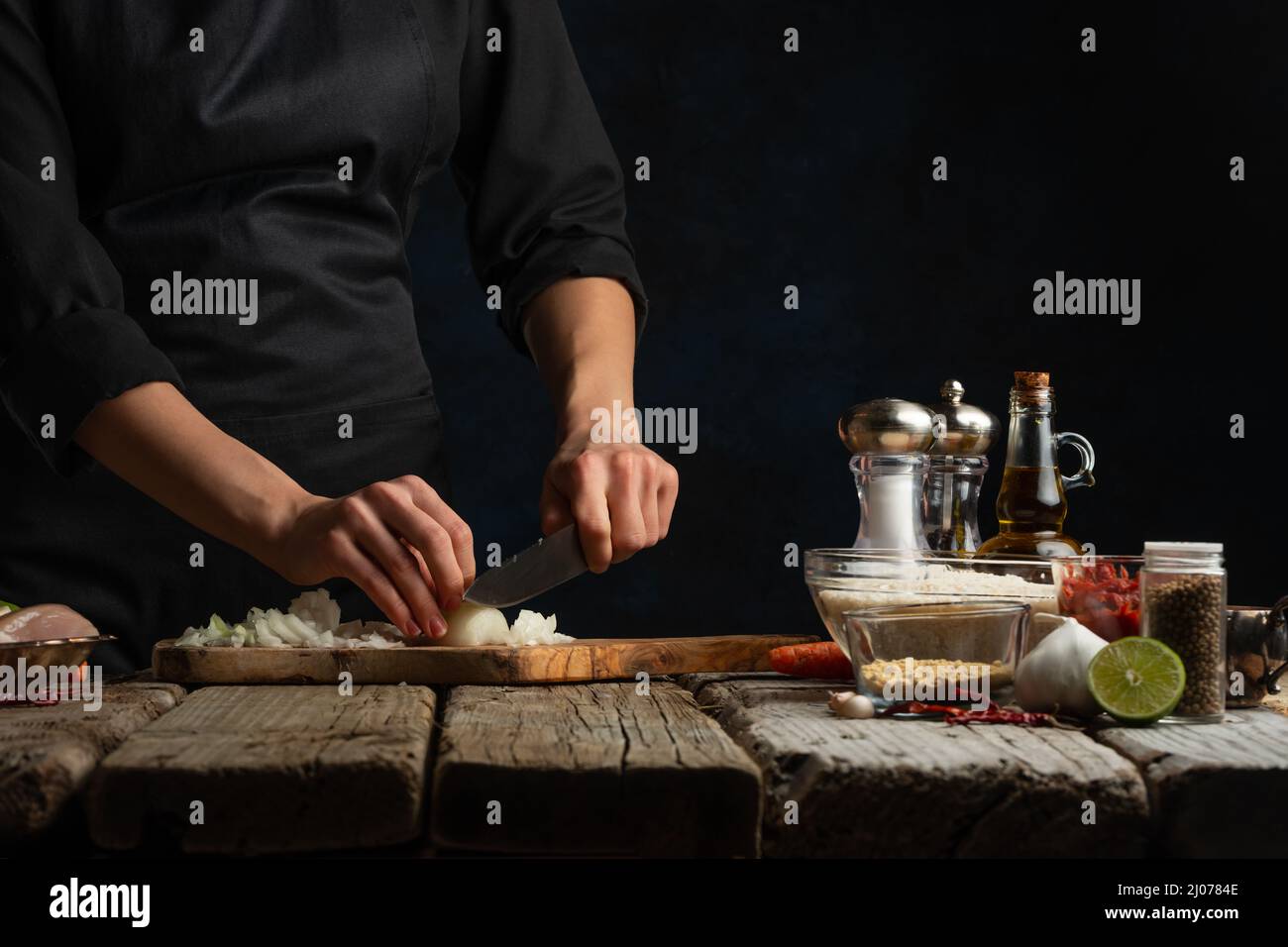 Professional chef cuts with knife onion on wooden chopped board ...