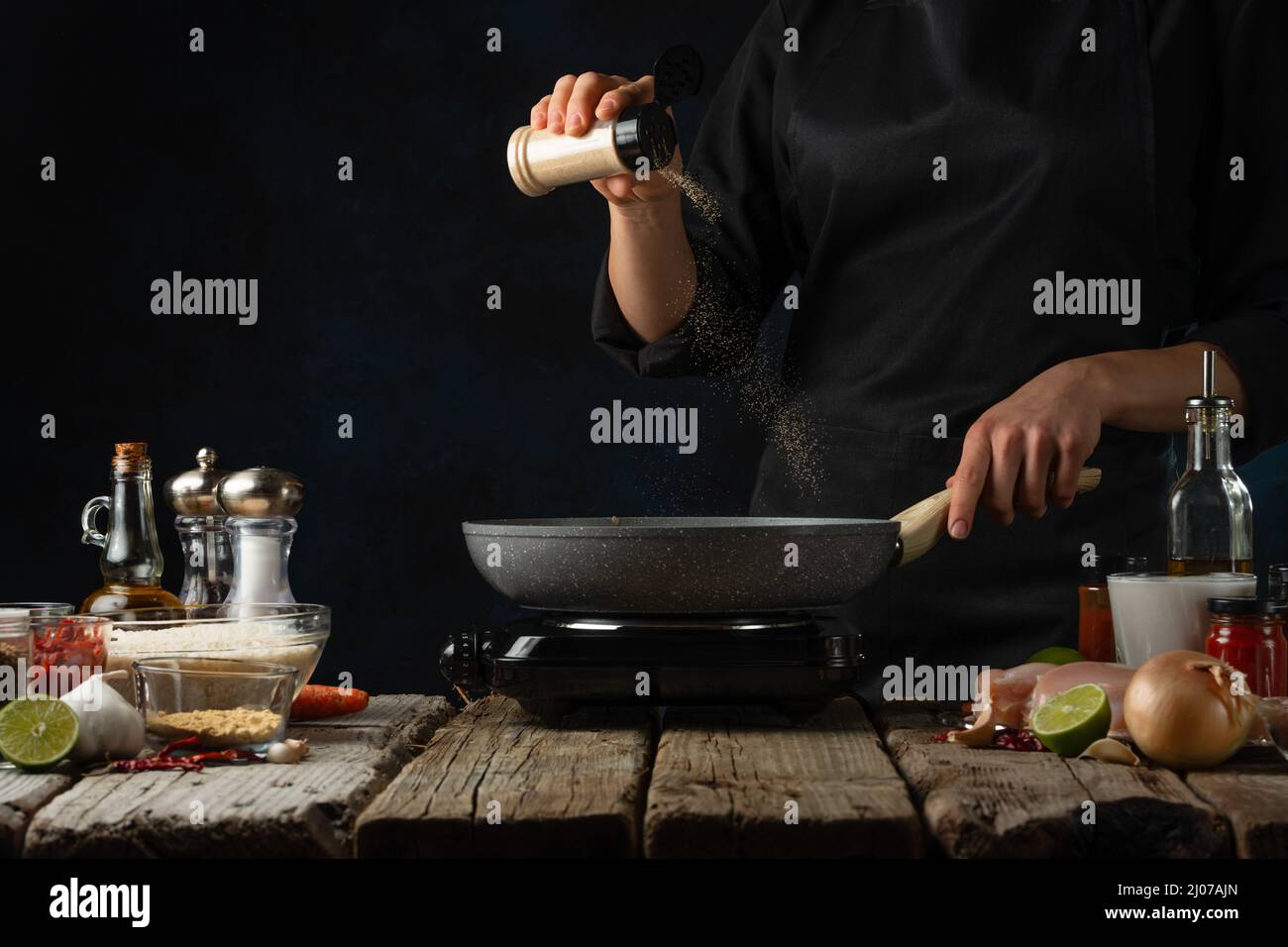 Professional chef pours spices into pan with frying chicken fillet ...