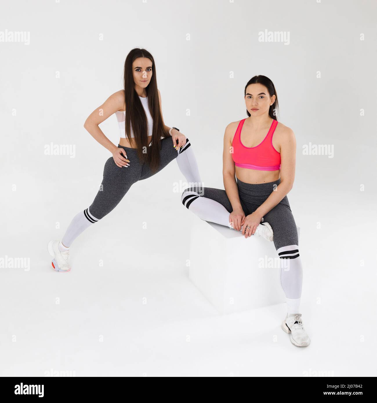 Two fitness young women posing in the studio with a cube on a white ...