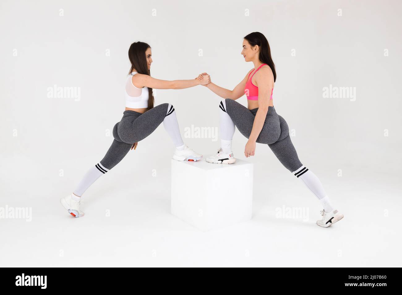 Two young fitness women give handshake on grey background in studio ...