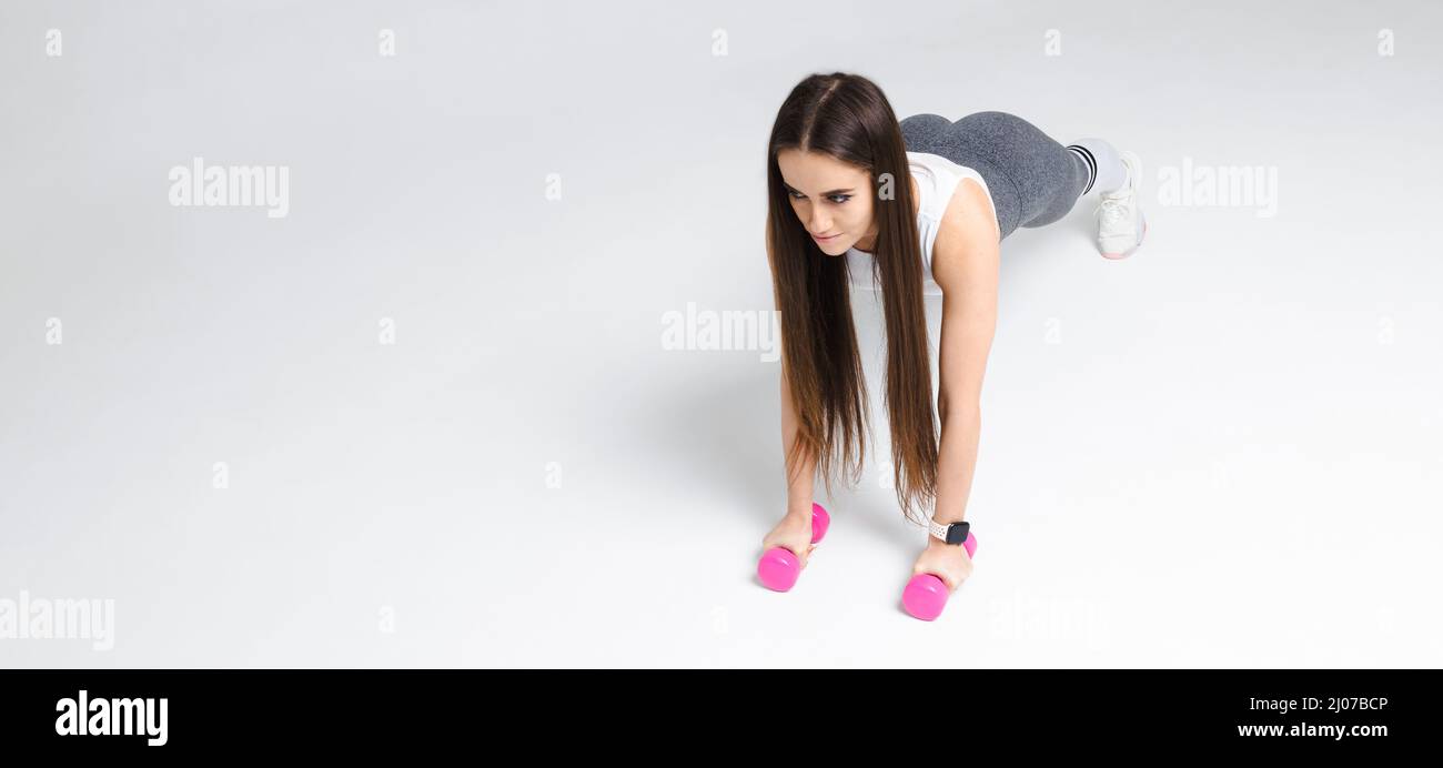 Pretty fitness girl doing push-ups or plank with dumbbells in the ...