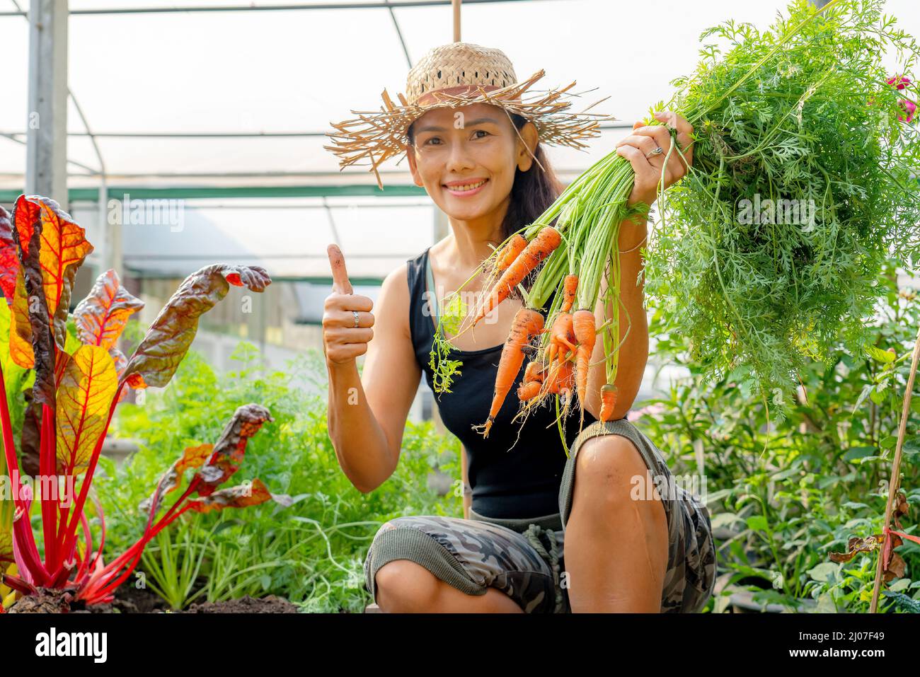 Happy woman with bunch of freshly harvested carrots in the backyard ...