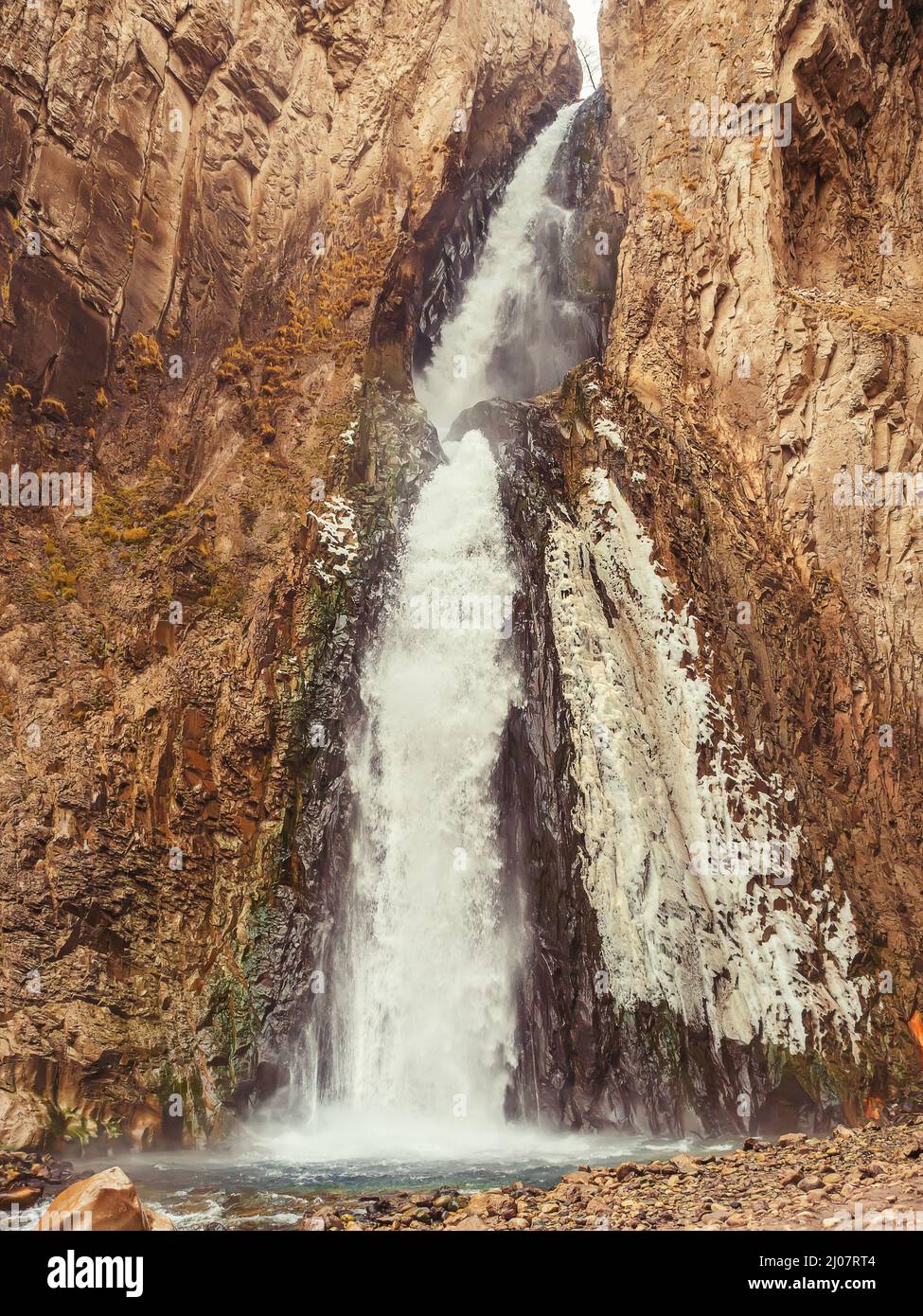 A huge powerful waterfall flows down between steep cliffs of the ...