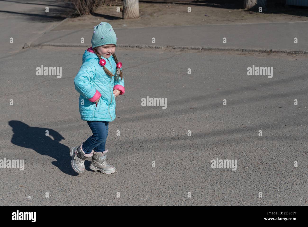 A child walks on an asphalt sidewalk. A five-year-old girl with her ...