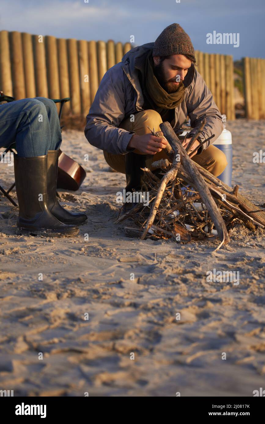Hell get it started. A young man building a fire on the beach Stock ...