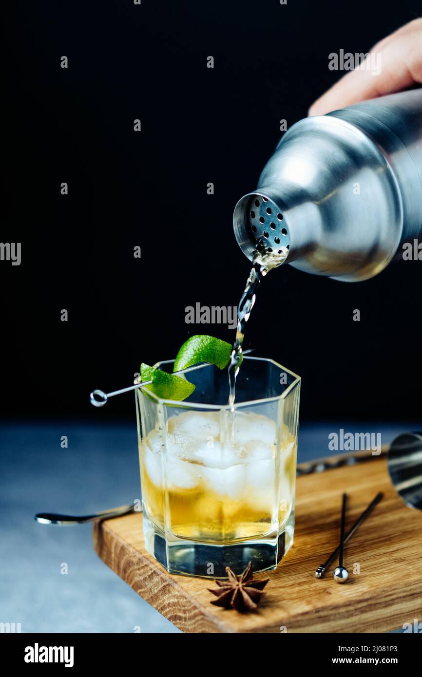 Alcohol cocktail pouring from shaker into gless with lime peel ice on ...