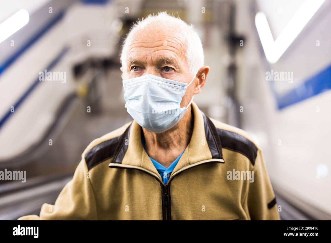 Elderly man in protective mask moving up on escalator while leaving ...