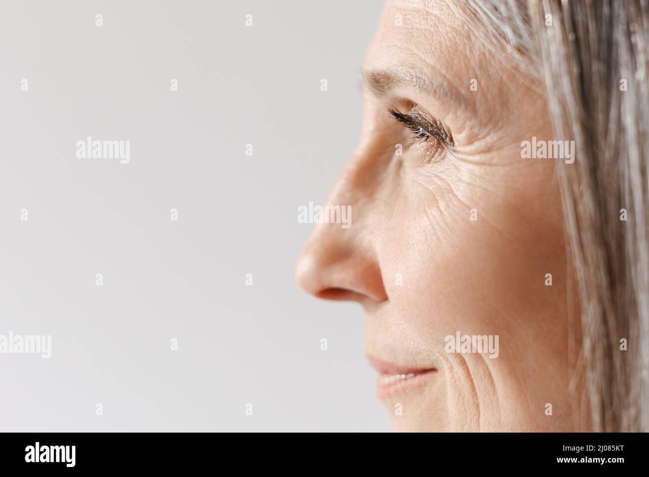 Grey senior woman smiling and looking aside while posing in profile ...