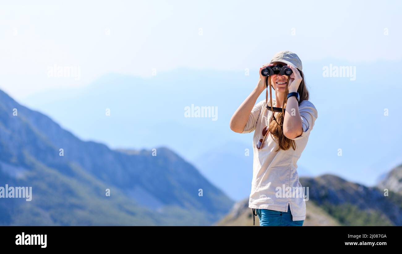 Young woman watching mountain landscape through binoculars at the view ...