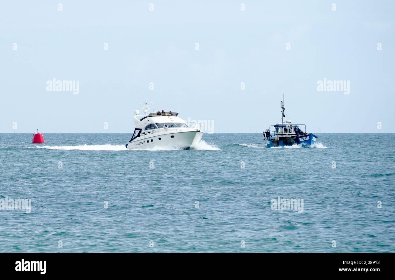 A small fishing boat and a leisure cruiser sailing parallel together at ...