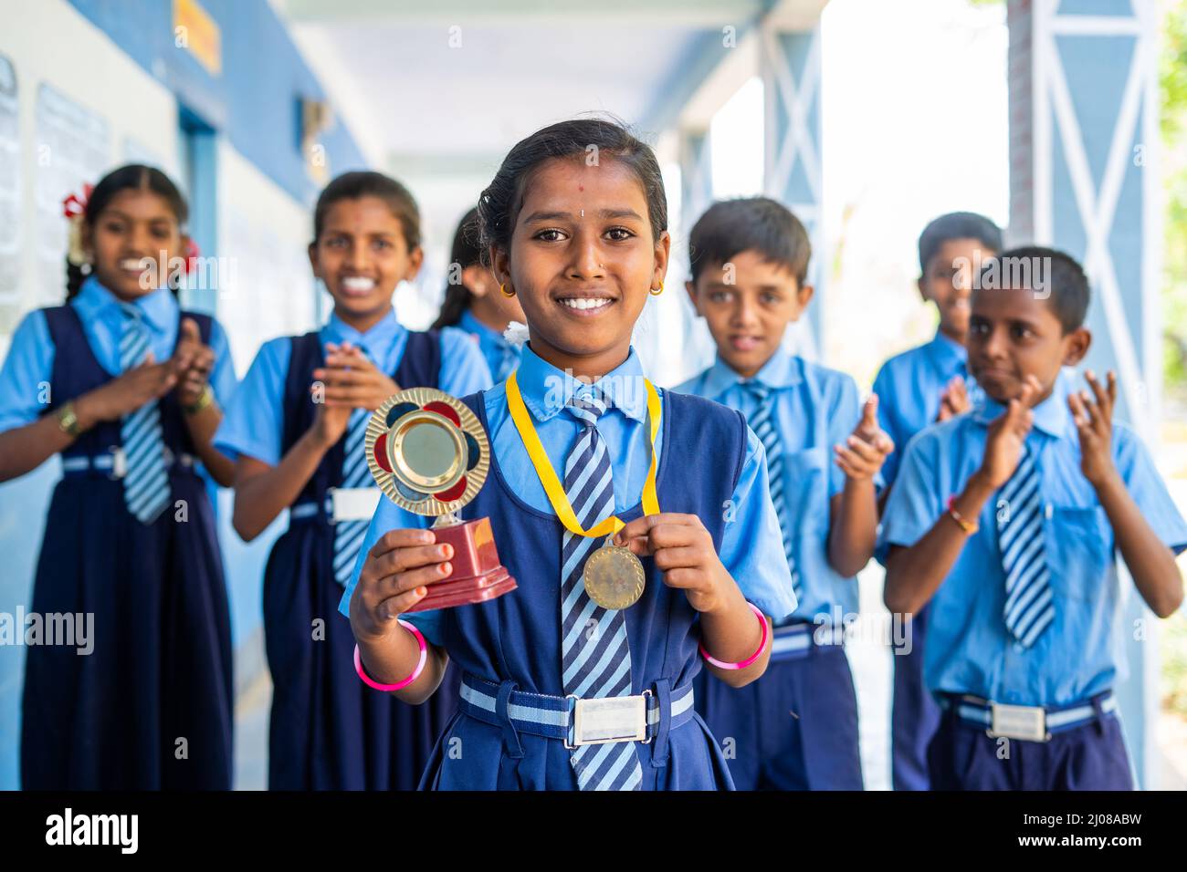 Proud girl with winner trophy and medal with cheeful students ...
