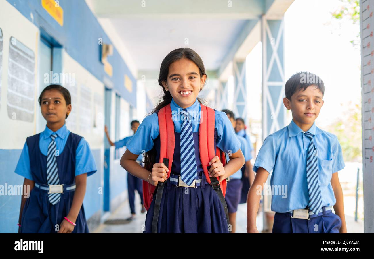 Happy girl kid in uniform standing at school corridor while other kids ...