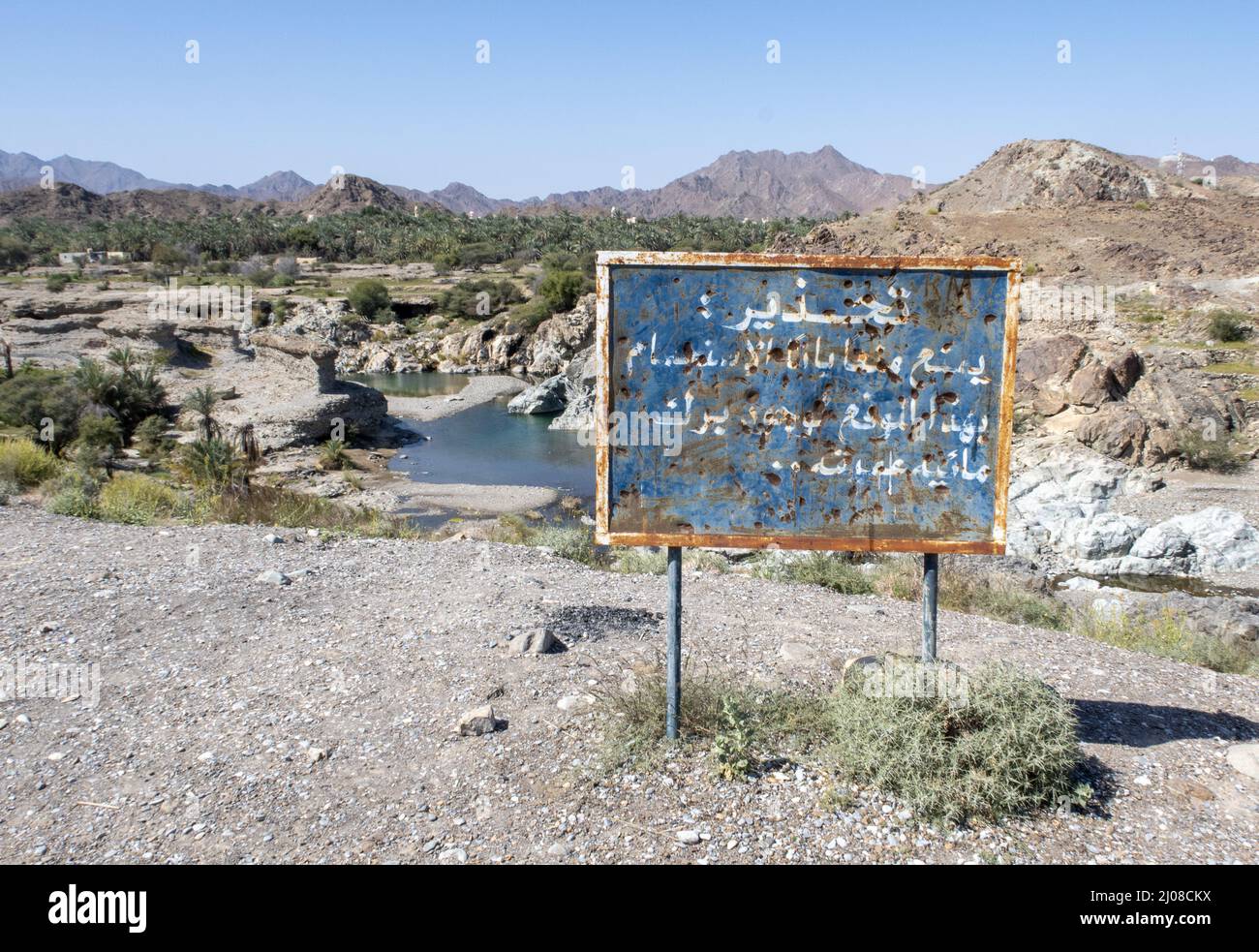 Old rusty blue sign with a warning white text in Arabic in bright ...