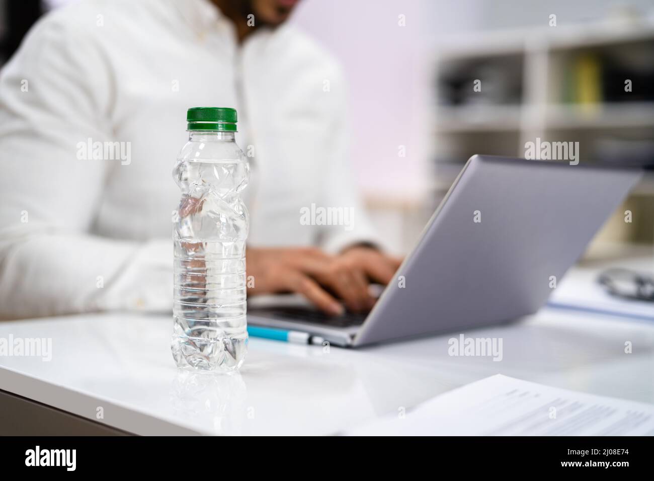 Water Bottle On Desk And Man In Foreground Using Computer Stock Photo ...