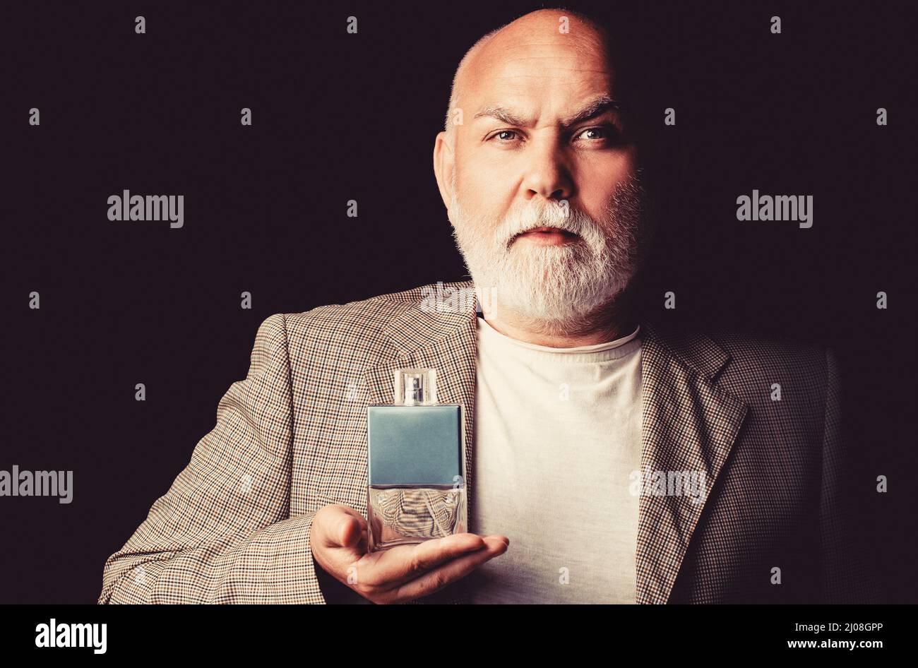 Masculine perfume, bearded old man in suit. Male holding up bottle of ...