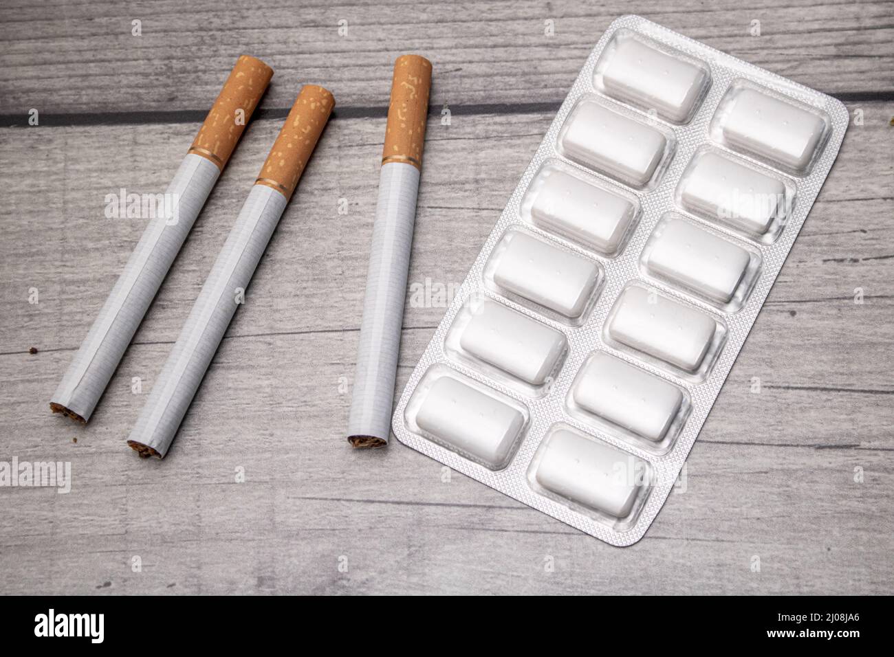 A blister pack with nicotine gum and three cigarettes on a wooden ...