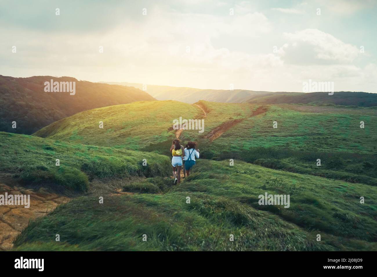 Two Latina teen friends run together holding hands down a country road ...