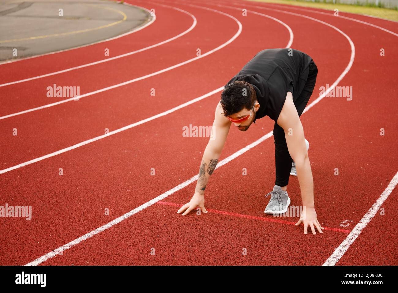 Sporty young man in sunglasses getting ready to run at stadium Stock ...