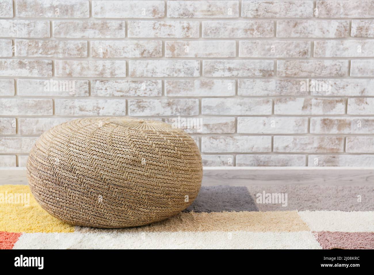 Modern pouf near light brick wall in room Stock Photo - Alamy