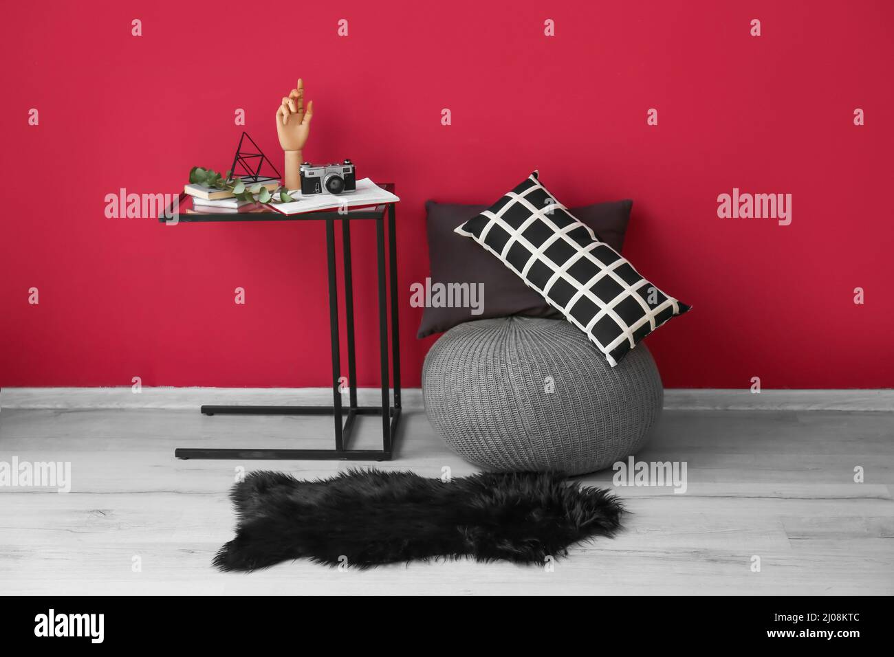Modern pouf and table near color wall in room Stock Photo - Alamy
