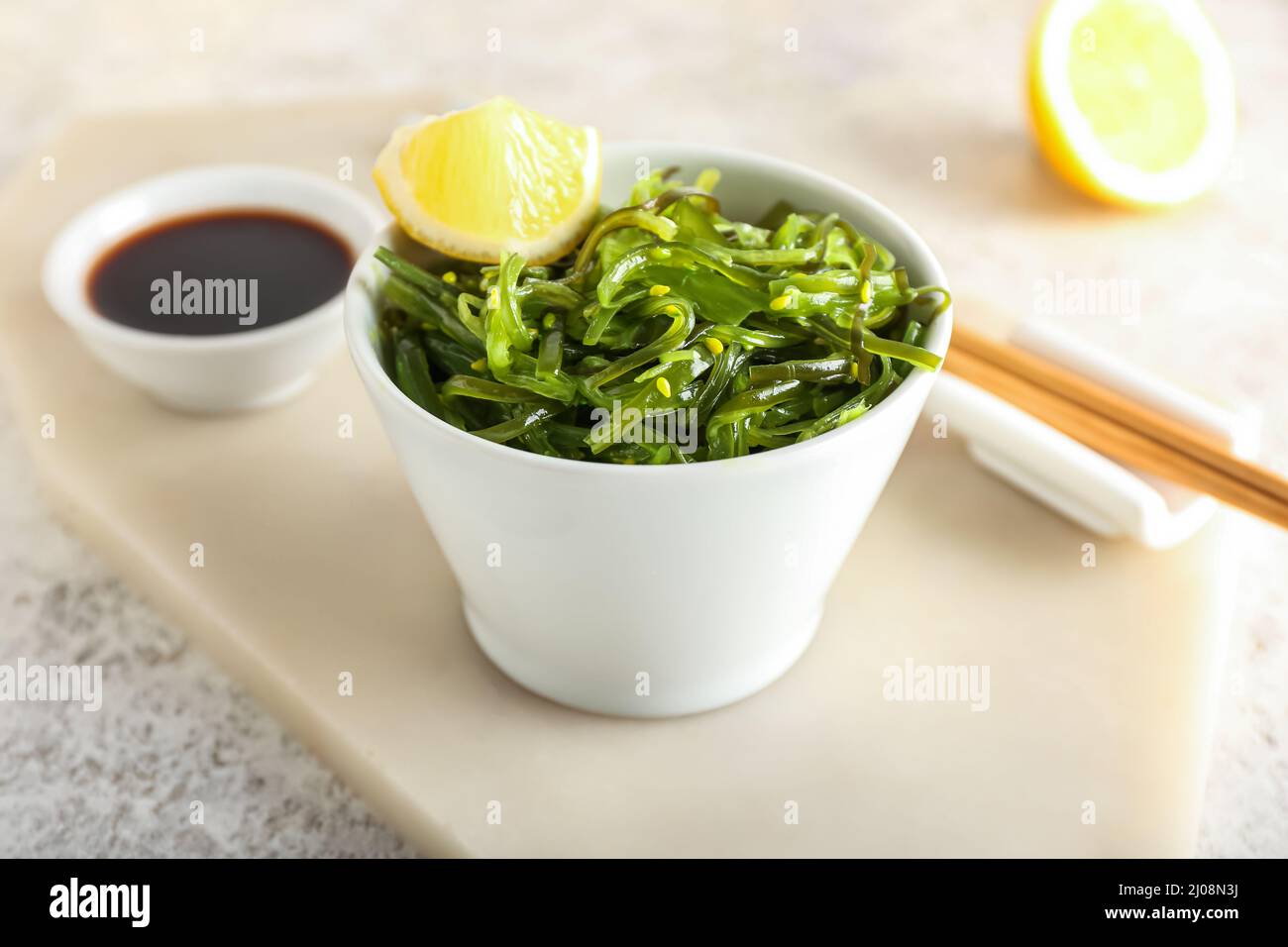 Bowl with healthy seaweed salad, lemon and sauce on light background ...