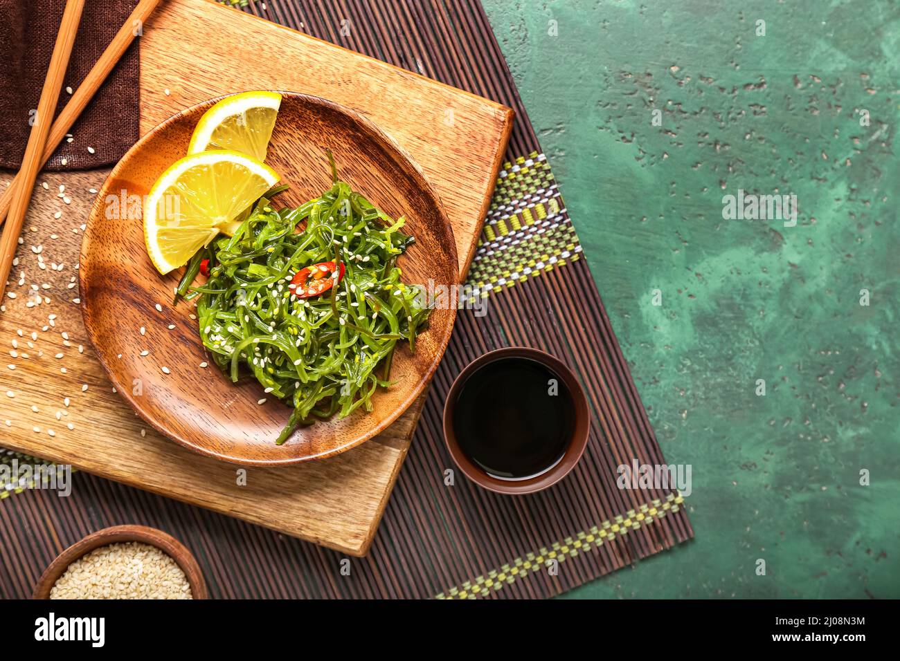 Plate with healthy seaweed salad, lemon and sauce on green background ...
