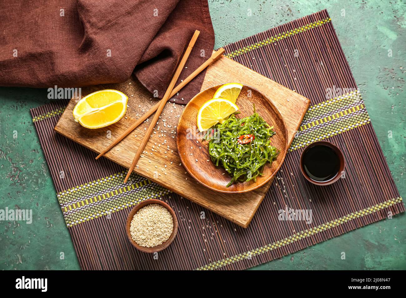 Plate with healthy seaweed salad, lemon and sauce on green background ...
