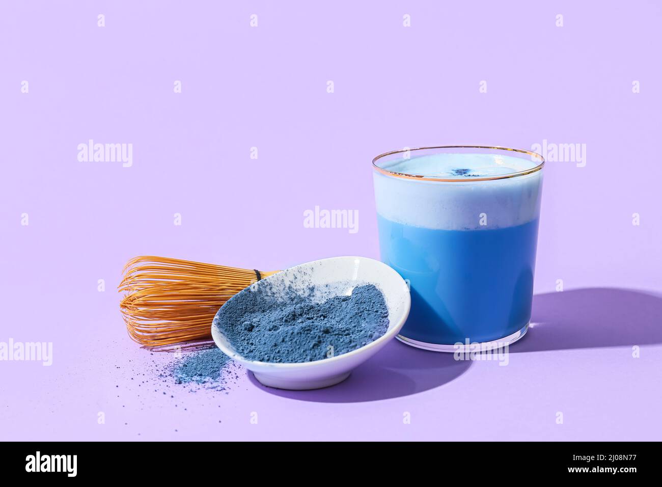 Glass of blue matcha tea, chasen and bowl with powder on purple ...
