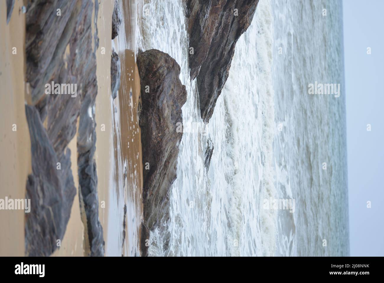 Vertical shot of rocky beach against the ocean waves on a cloudy day ...