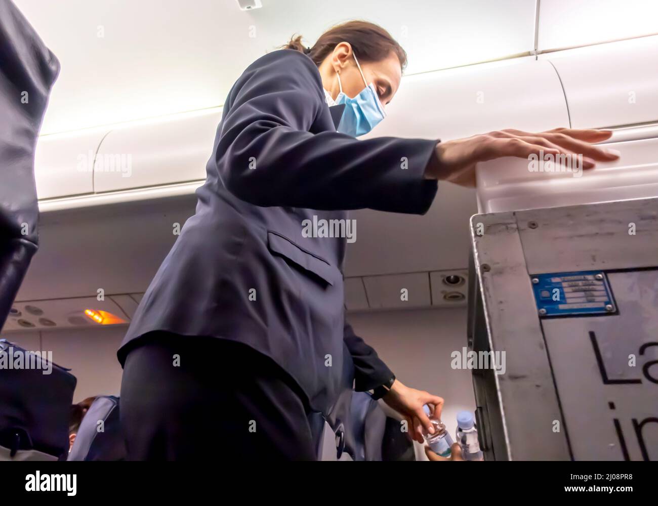 Female flight attendant in face mask serving water drinks to passengers ...