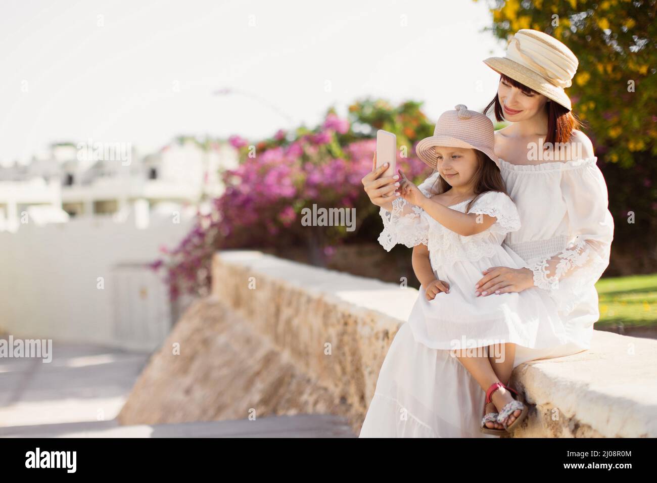 Happy traveler mother and her daughter in white dresses using mobile ...