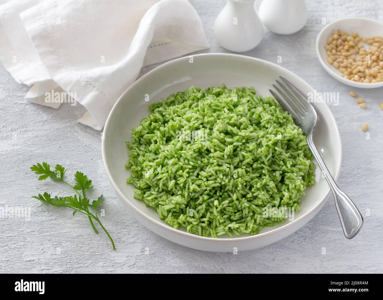 Vegan rice with green oil and pine nuts in a white bowl on a gray ...