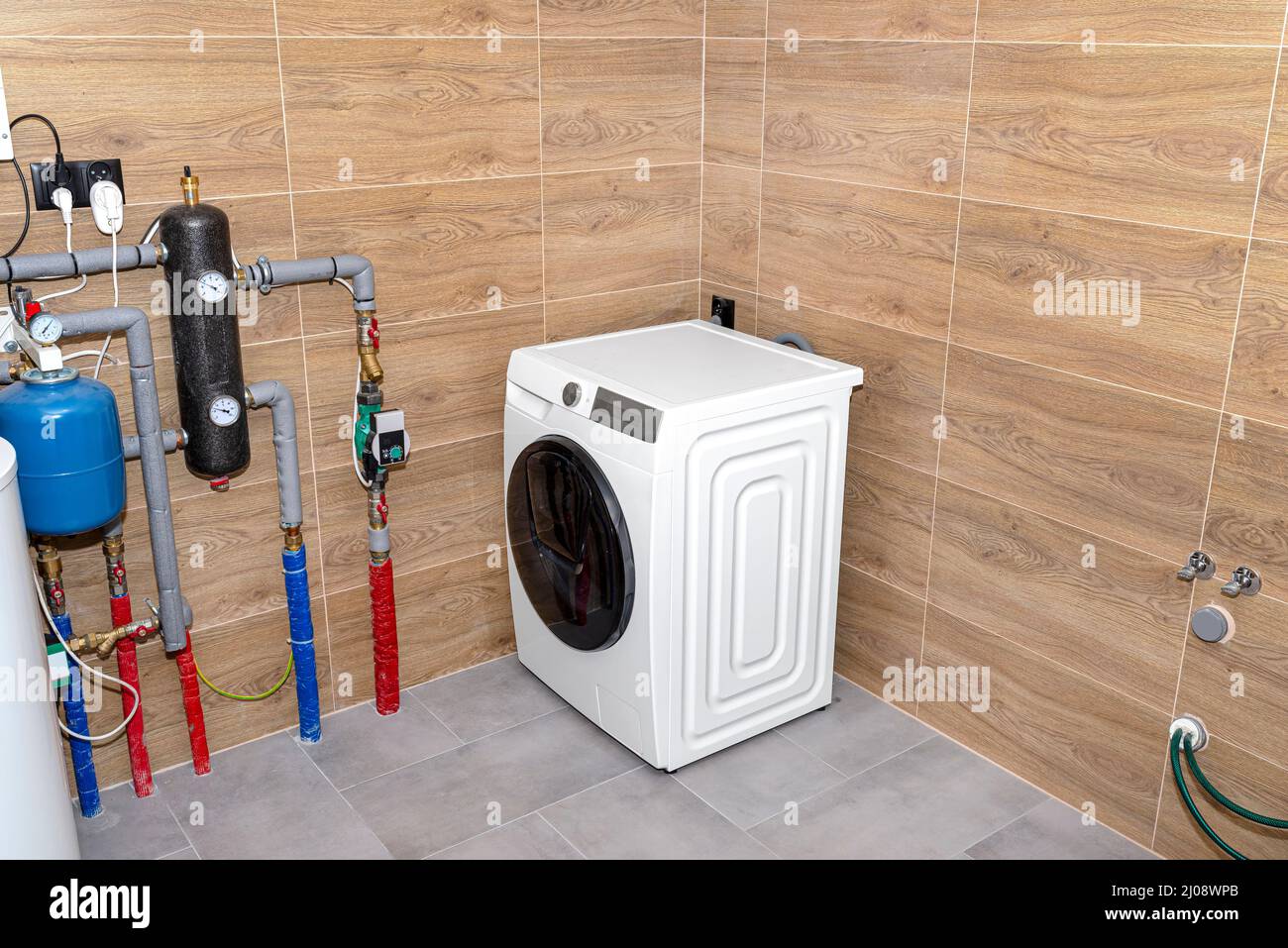 A washing machine standing in the corner of a modern gas boiler room ...