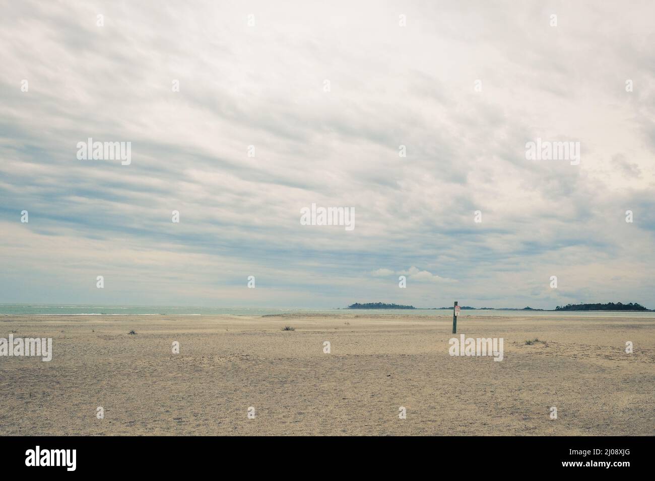 Distant land on horizon seen from sandy beach with dramatic clouds in ...