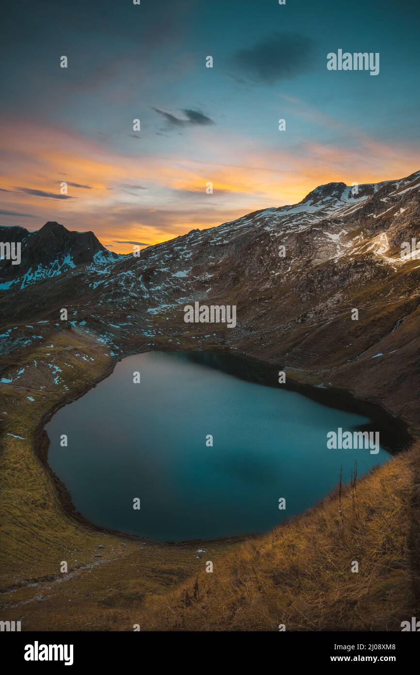 Vertical shot of a tranquil lake surrounded by mountains during sunset ...