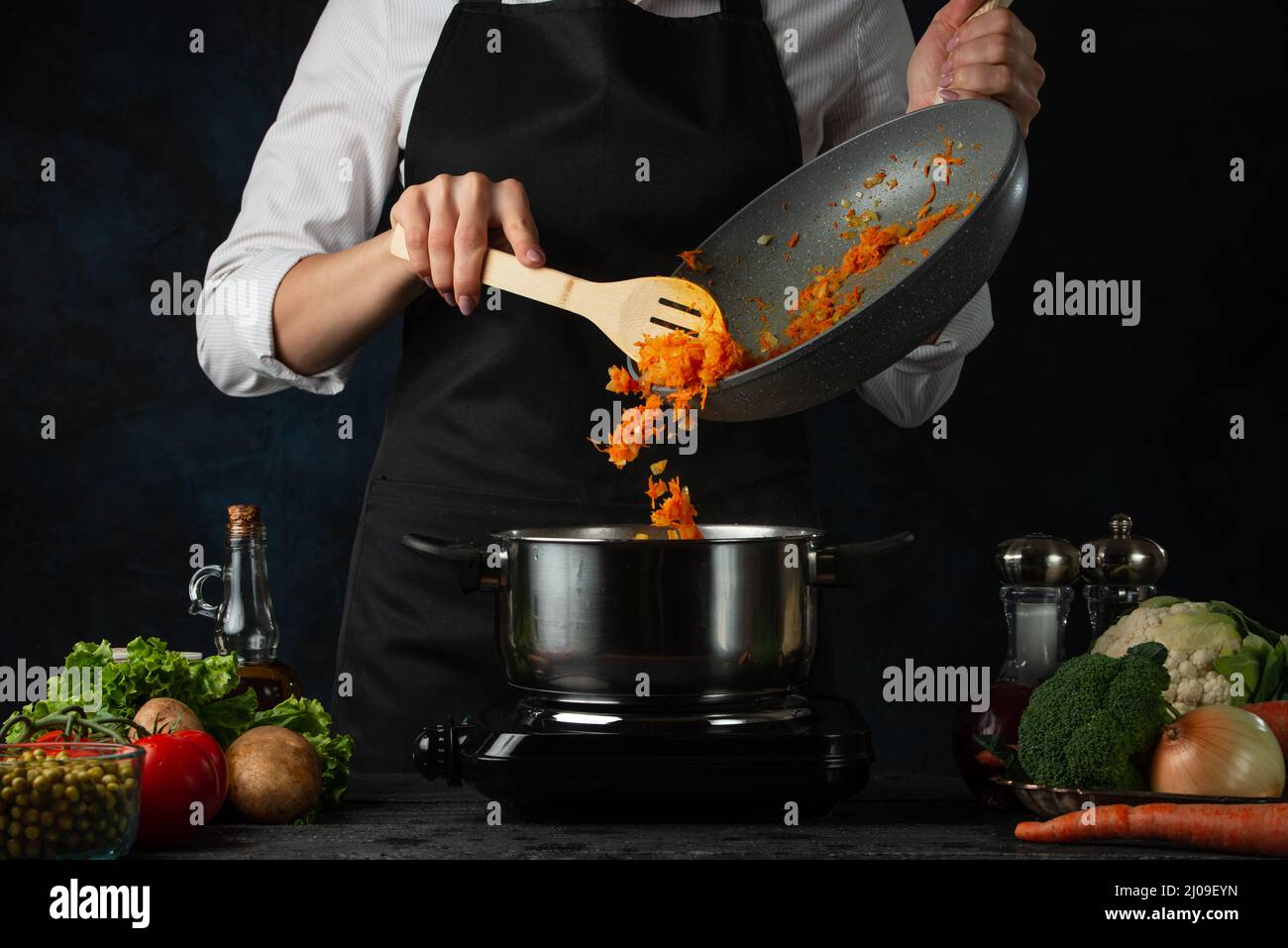 Professional chef pours frying vegetables into pan for cooking soup on ...