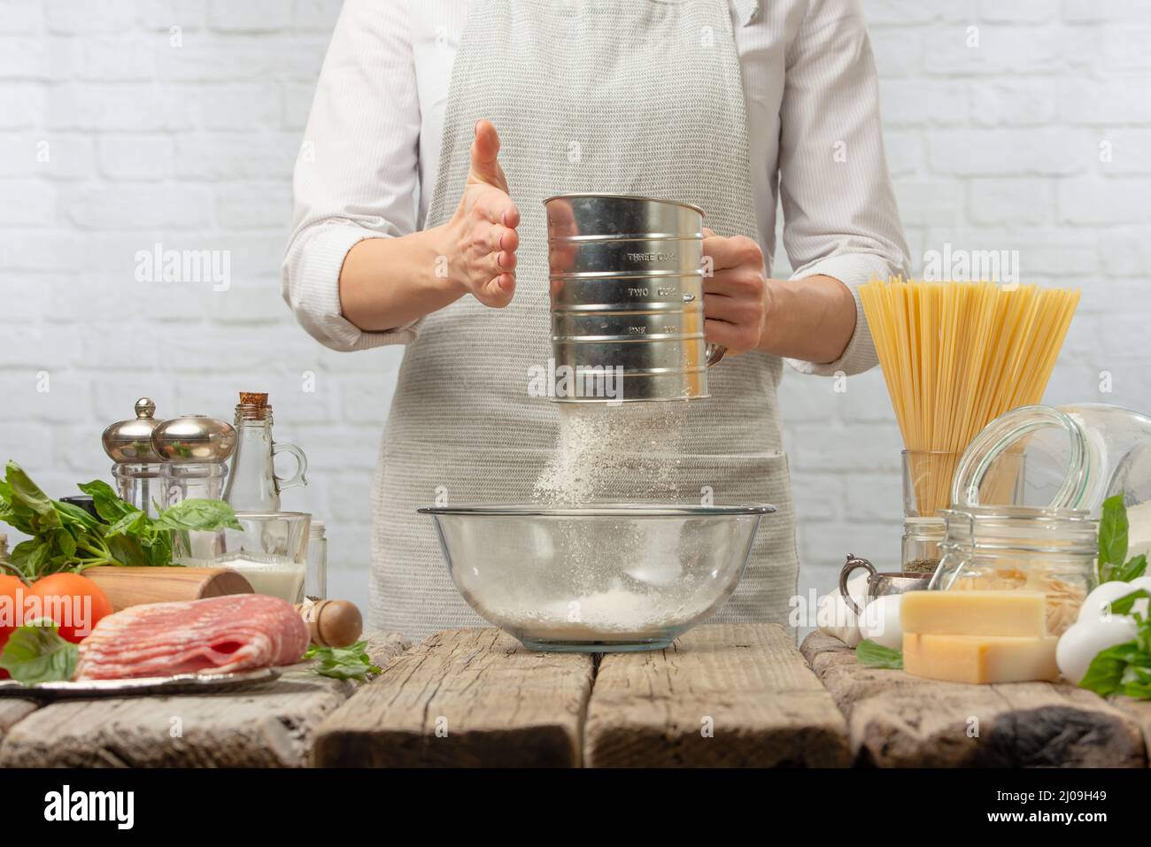Professional chef in white uniform sifts flour into glass bowl for ...