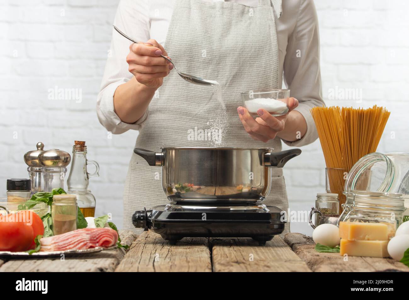 Chef in white uniform salts boiling water. Backstage of cooking pasta ...