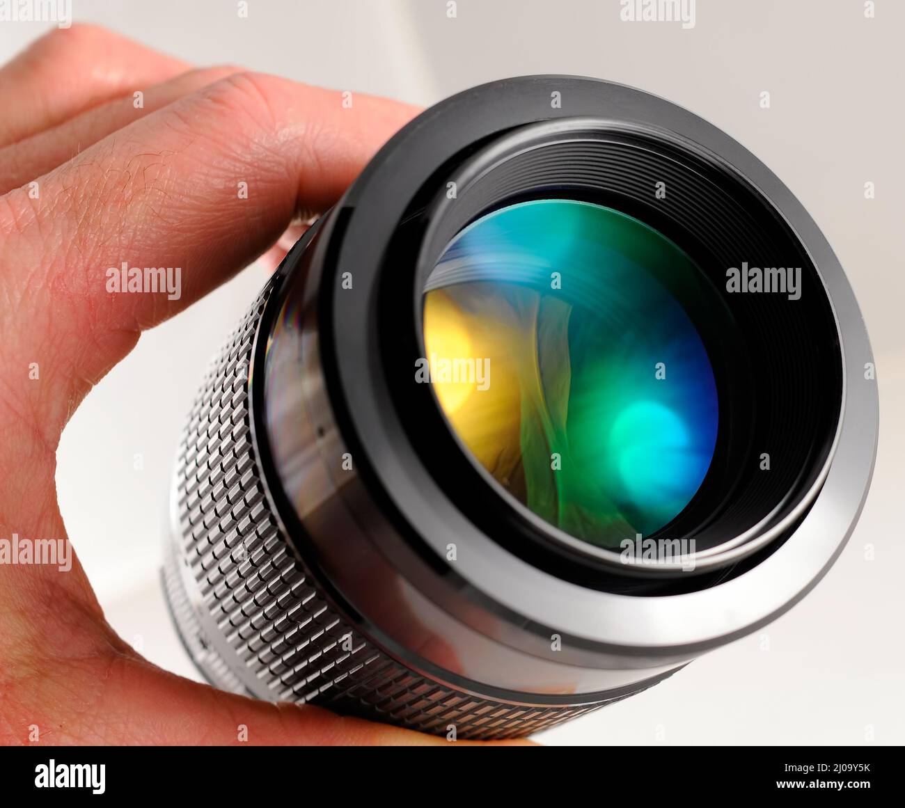 hand holding lens with colorful reflections on front glass element ...