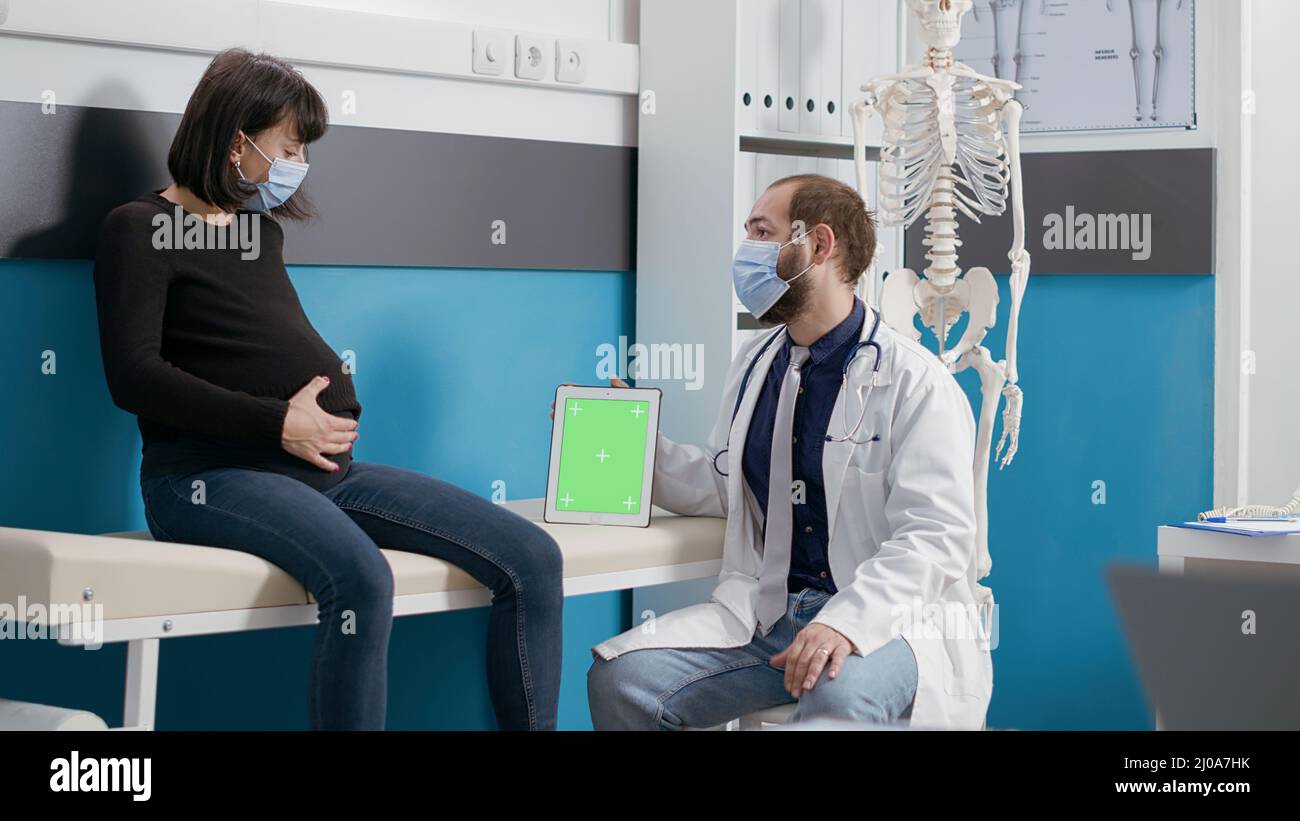 Pregnant woman and doctor looking at green screen on digital tablet ...
