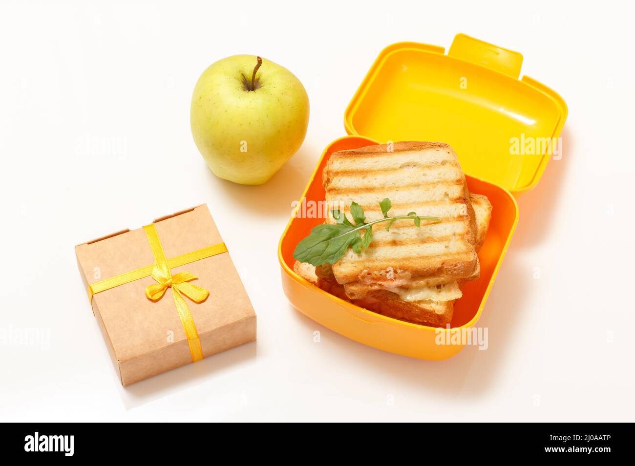 Yellow lunch box with toasted slices of bread, cheese, a green apple ...
