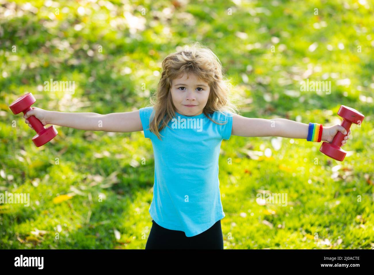 Cute little boy doing exercises with dumbbells in green park. Portrait ...