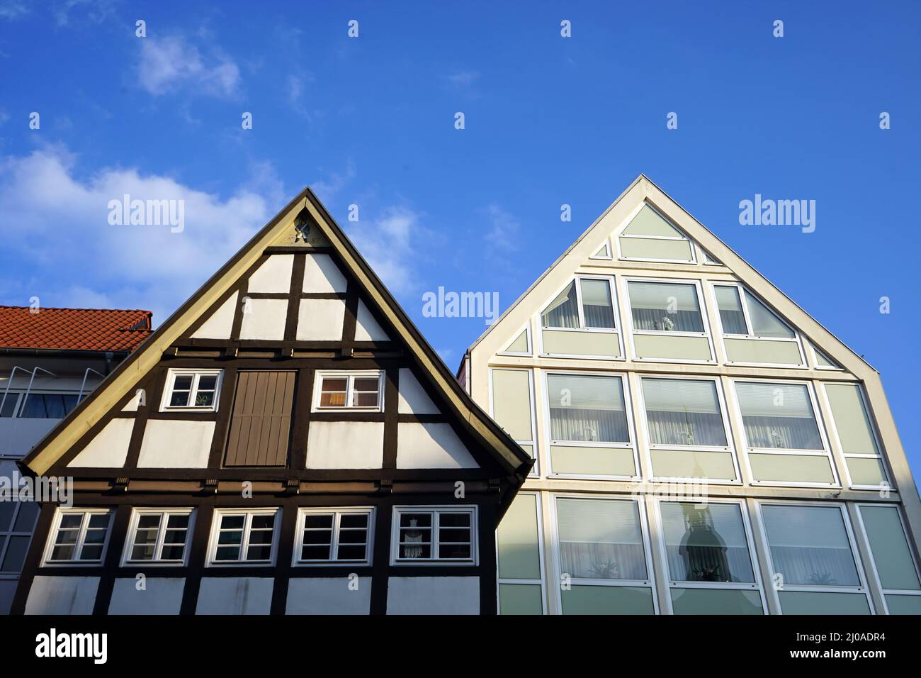 Facade of two houses with triangular roofs against a blue cloudy sky ...