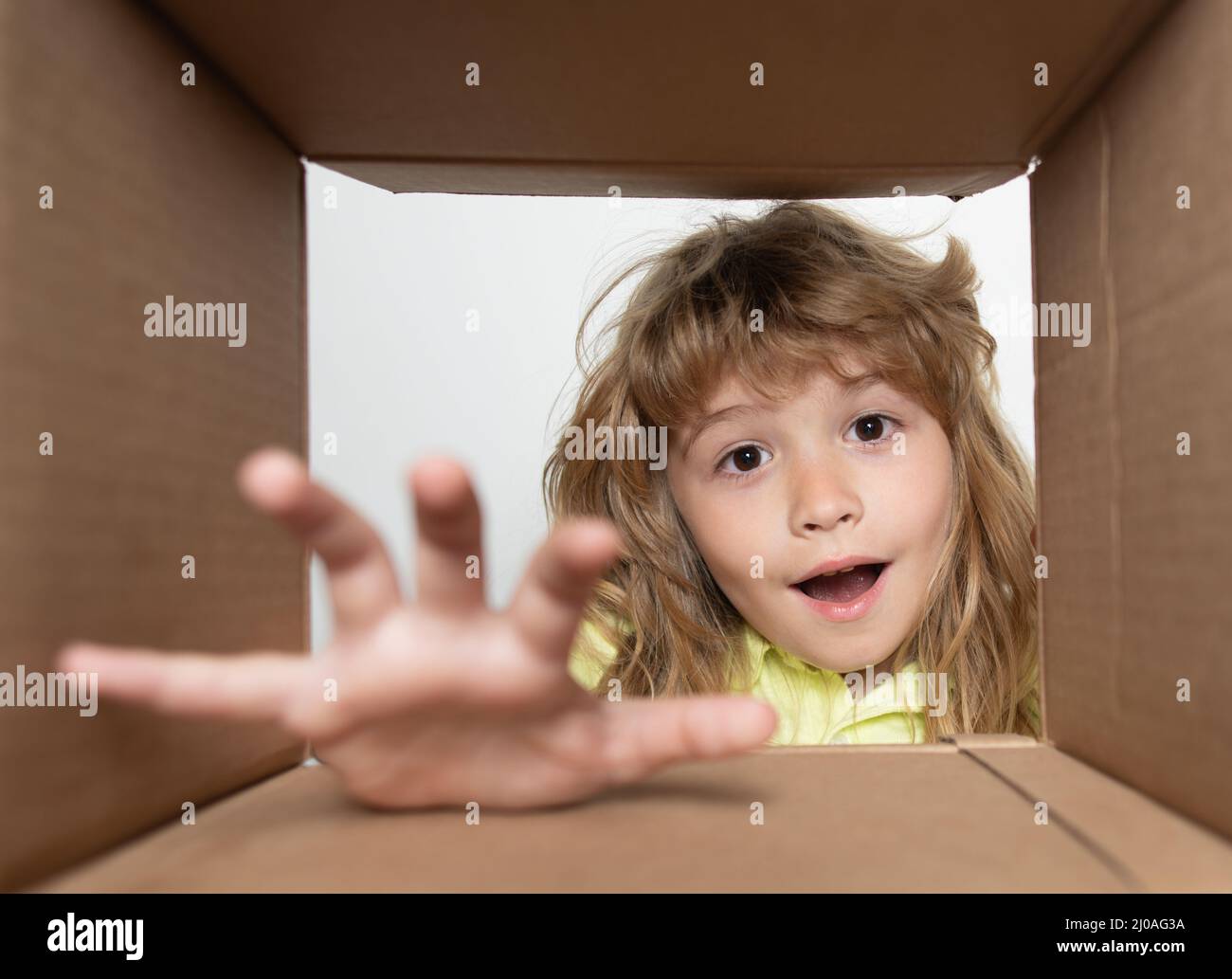 Funny excited child unpacking and opening the carton box looking inside ...