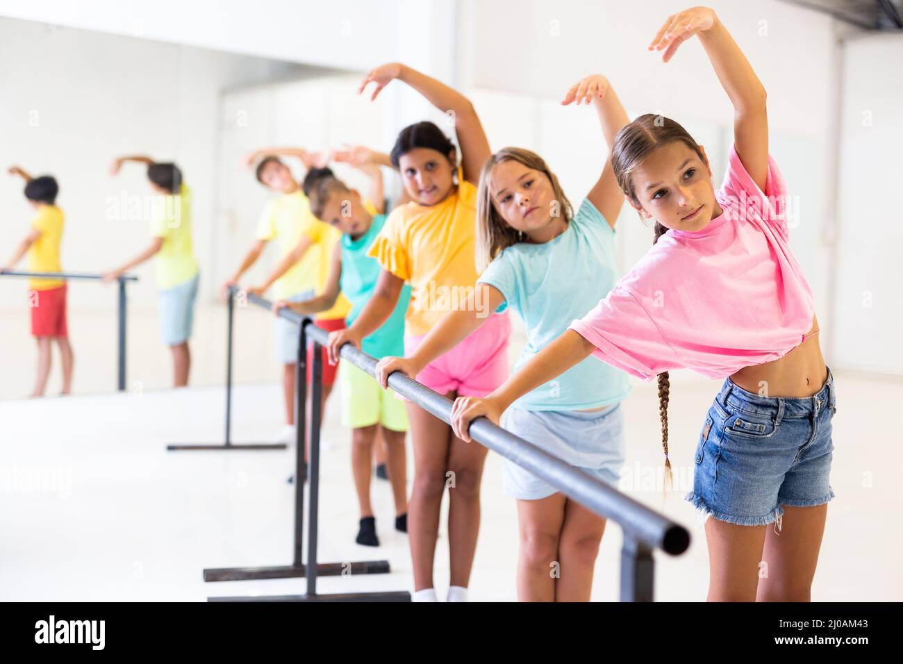 Diligent tween girl practicing classic dance moves near ballet barre ...