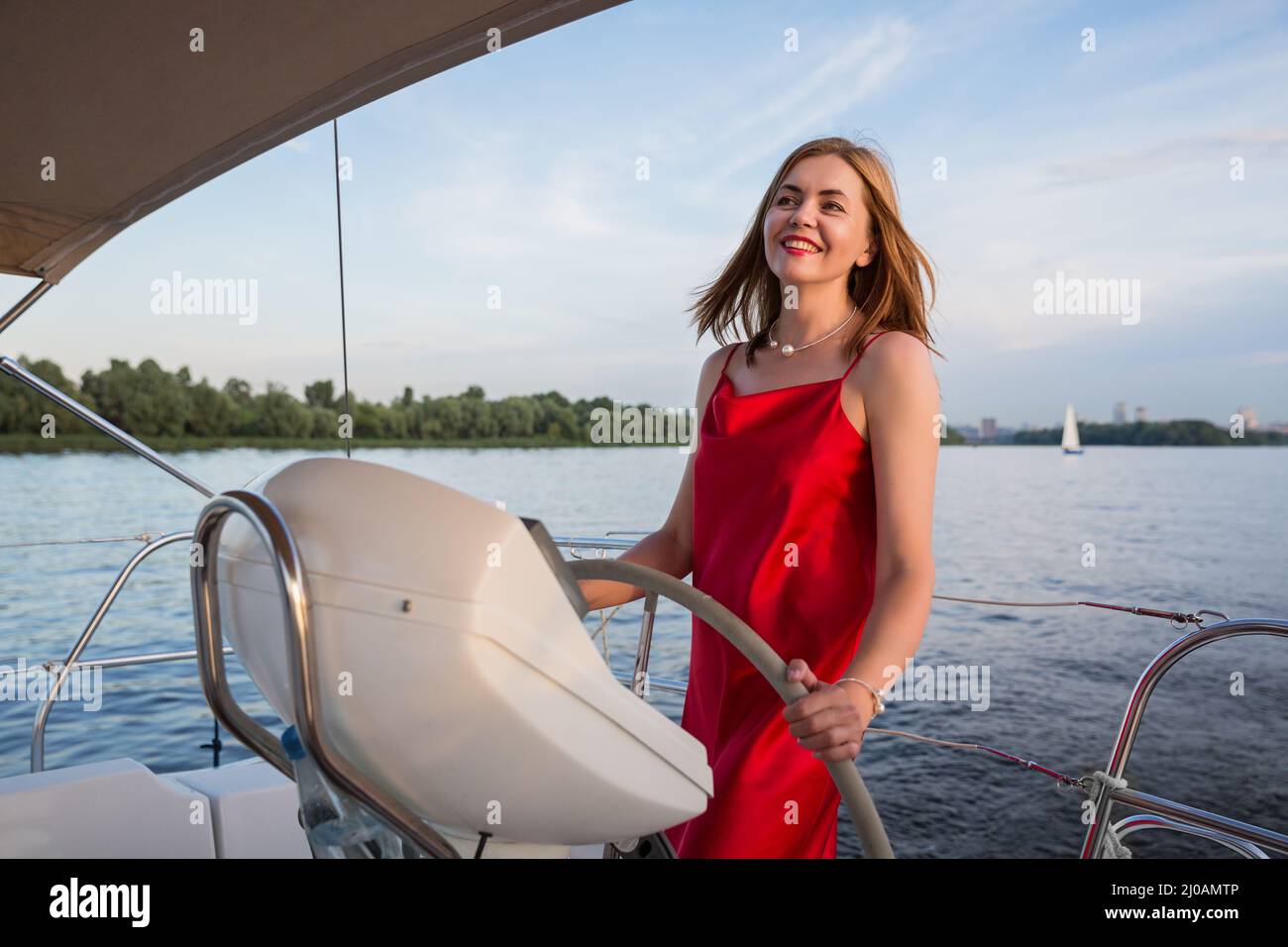 Pritty lady skipper in a long red dress holding the helm of the ship ...